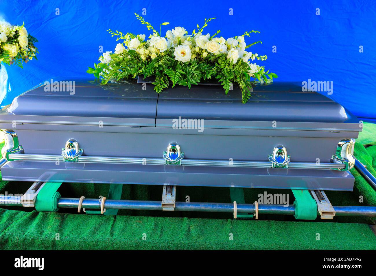 Funeral silver coffin casket with white flowers on green, creating solemn atmosphere during ...