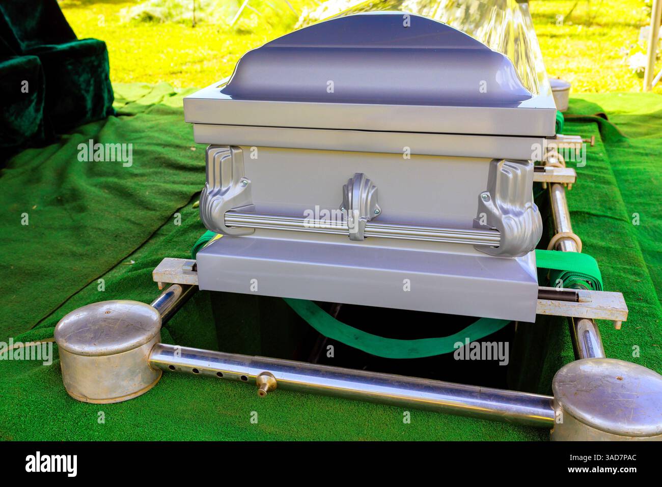 Silver coffin casket is placed above freshly dug grave with green grass, silent surroundings ...