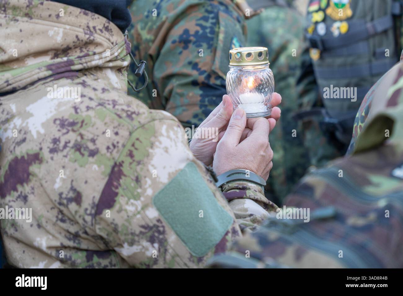 A soldier in camouflage holds candlestick at a military commemoration ...