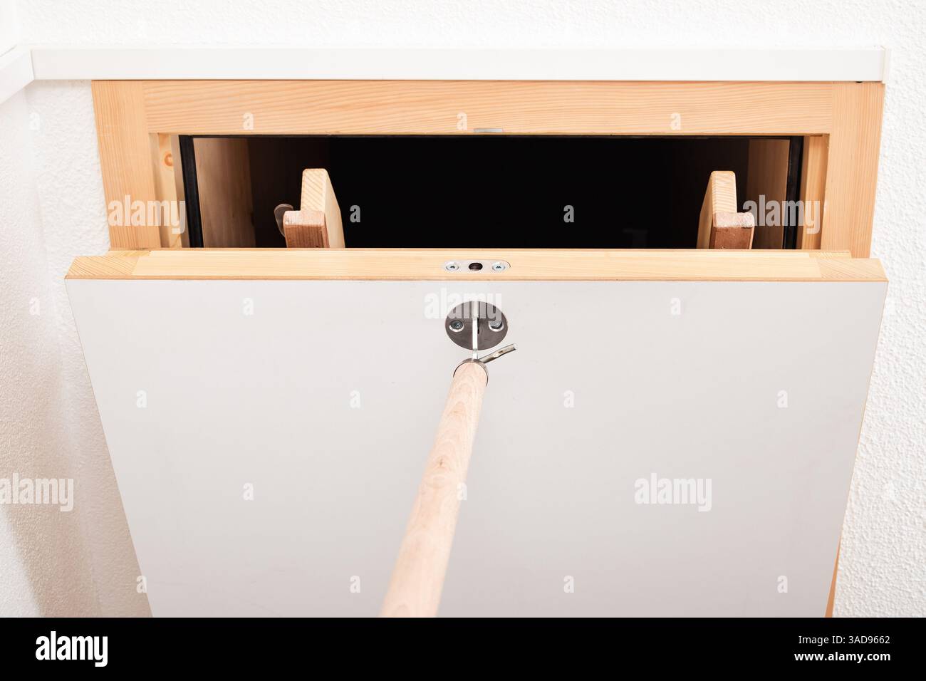 Attic hatch or loft door is opened with handle. Wooden extension pole ...