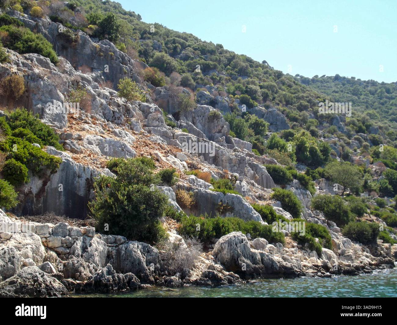 A rocky hillside covered with greenery, overlooking a calm body of ...