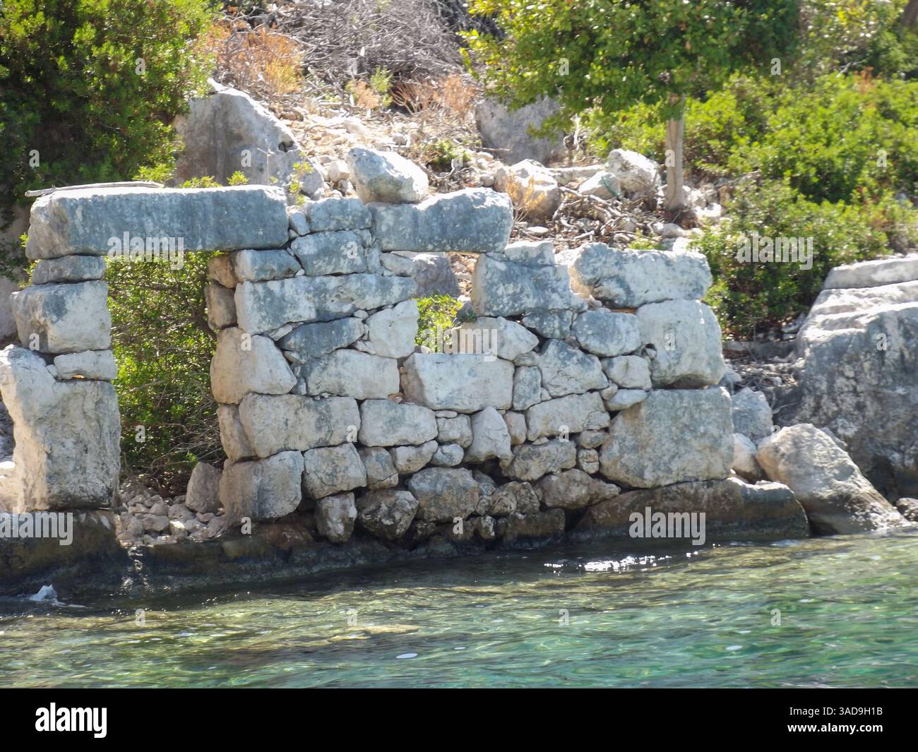A weathered stone wall partially submerged in clear water, surrounded ...