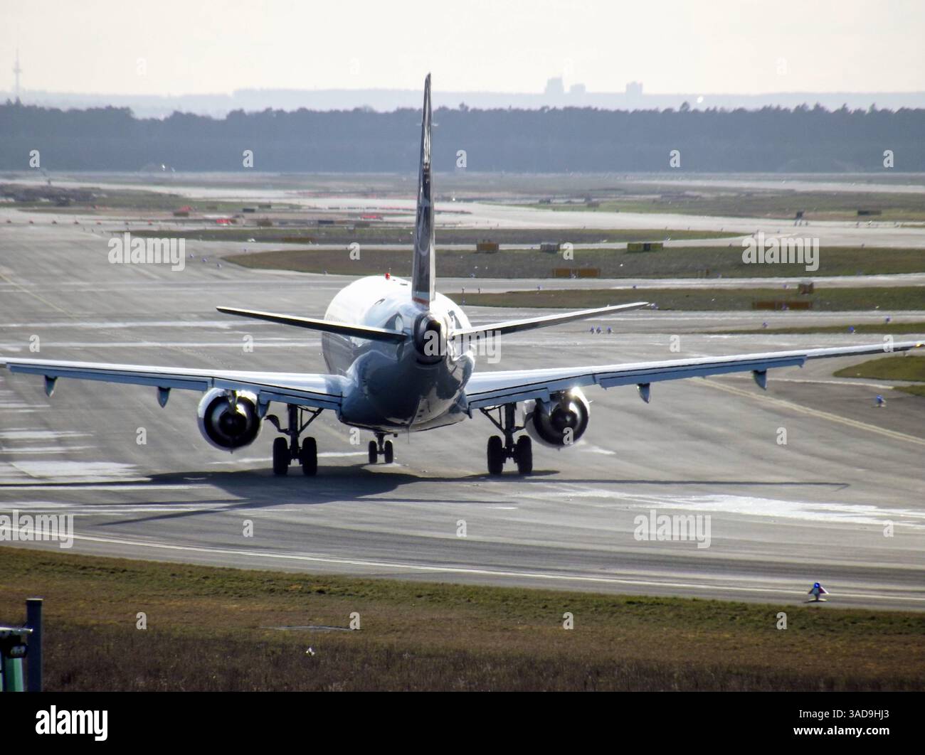A commercial airplane taxiing on a runway, with its rear view visible ...