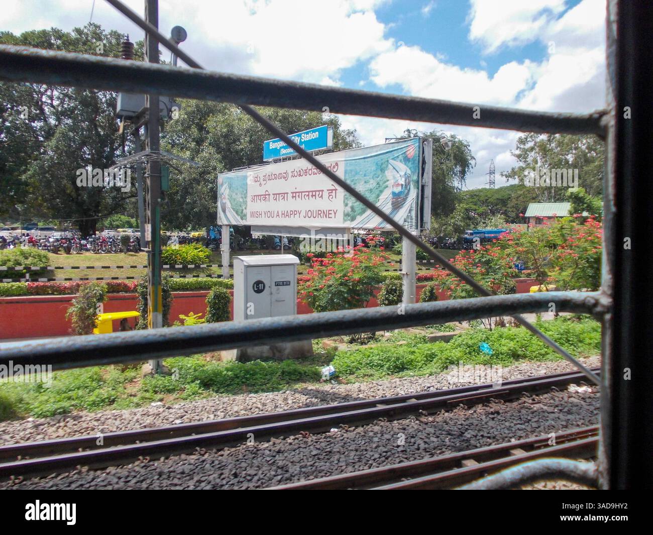 A view from a train window showing a railway station with greenery and ...