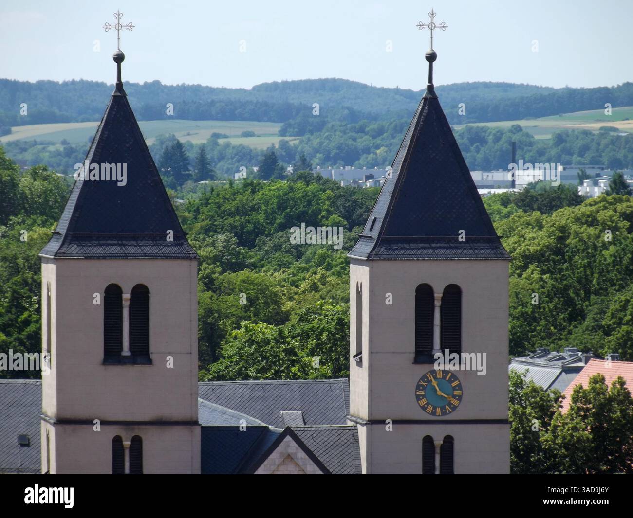 Two church towers with pointed roofs and a clock, surrounded by lush ...
