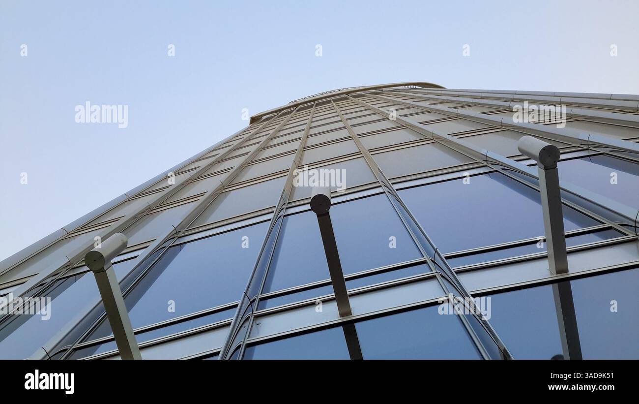 A low-angle view of a modern skyscraper with a glass facade and metal framework, reaching ...