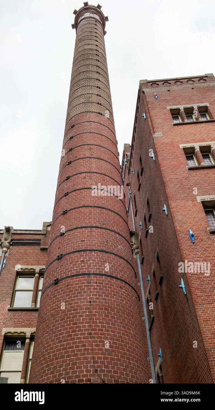A tall, cylindrical brick chimney rising alongside a red brick building ...