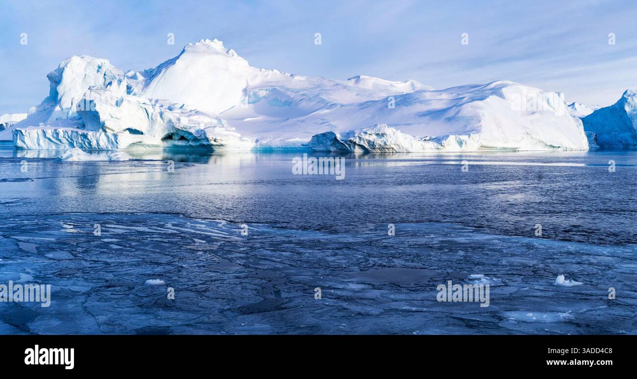 A serene landscape featuring large icebergs floating in calm waters, reflecting the blue sky ...