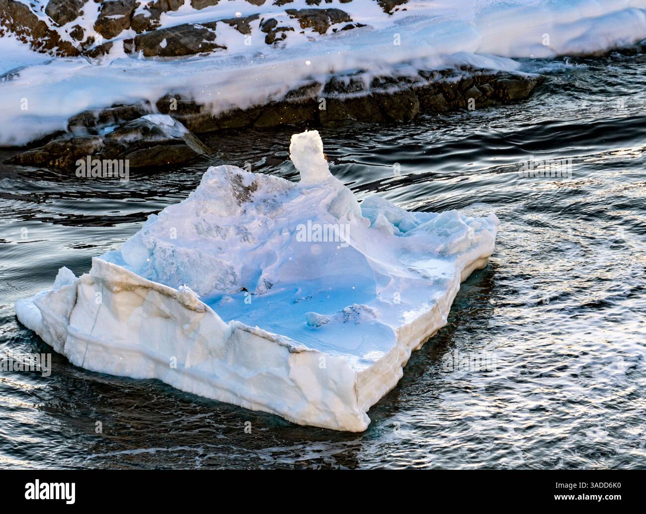 A large piece of ice floating in a body of water, surrounded by rocky ...