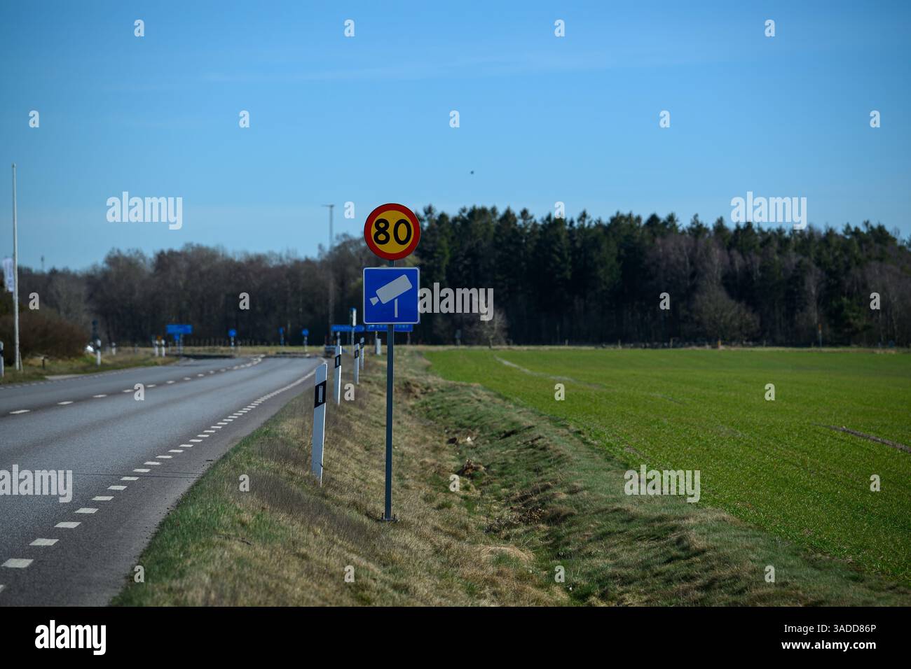 A notable speed limit sign stands beside a quiet country road, warning ...
