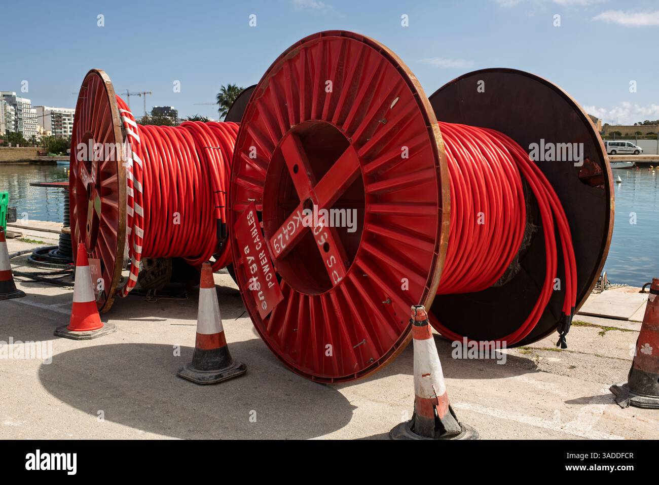Large red industrial cable reels on a port dock with a sea bay in the ...