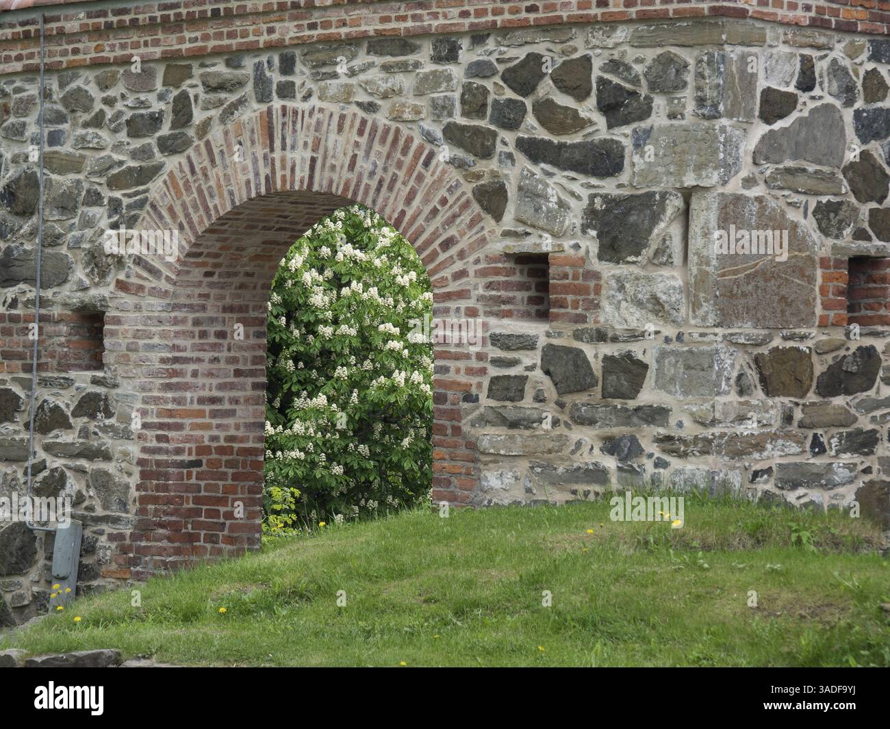 A round arch in a stone and brick wall opens onto a flowering garden ...
