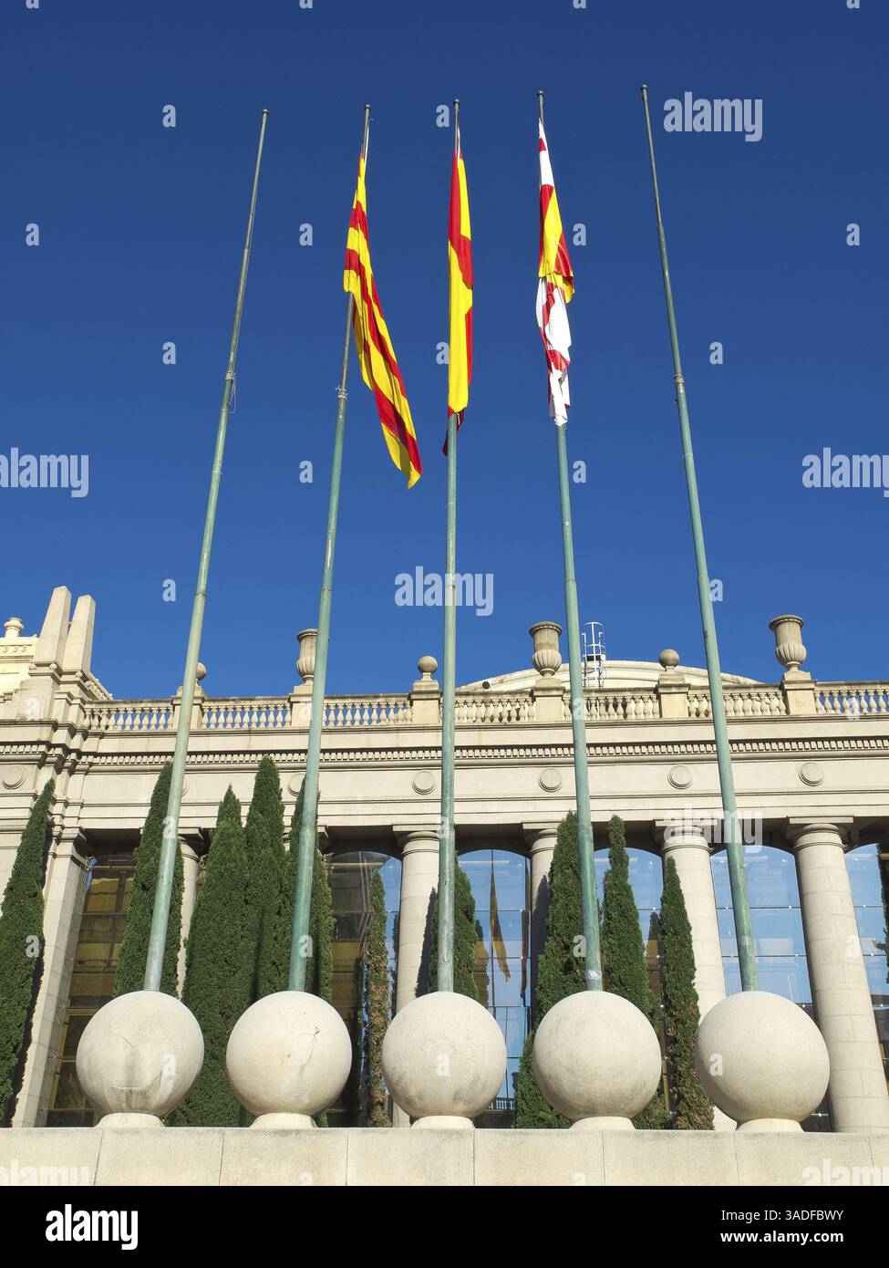 Five flags fly over a building with columns under a clear blue sky ...