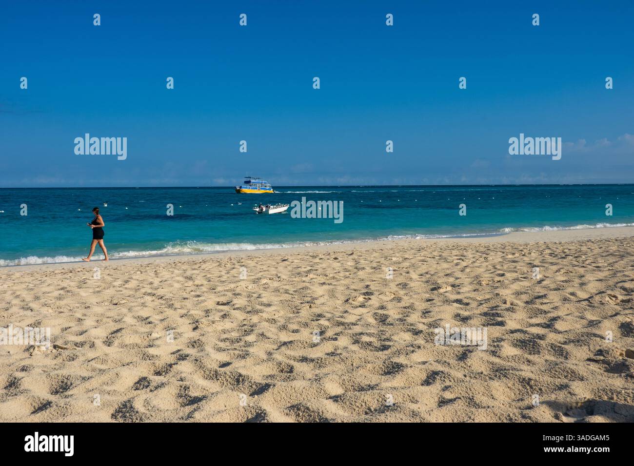 A woman strolls along Grace Bay Beach as tour boats sail the turquoise ...