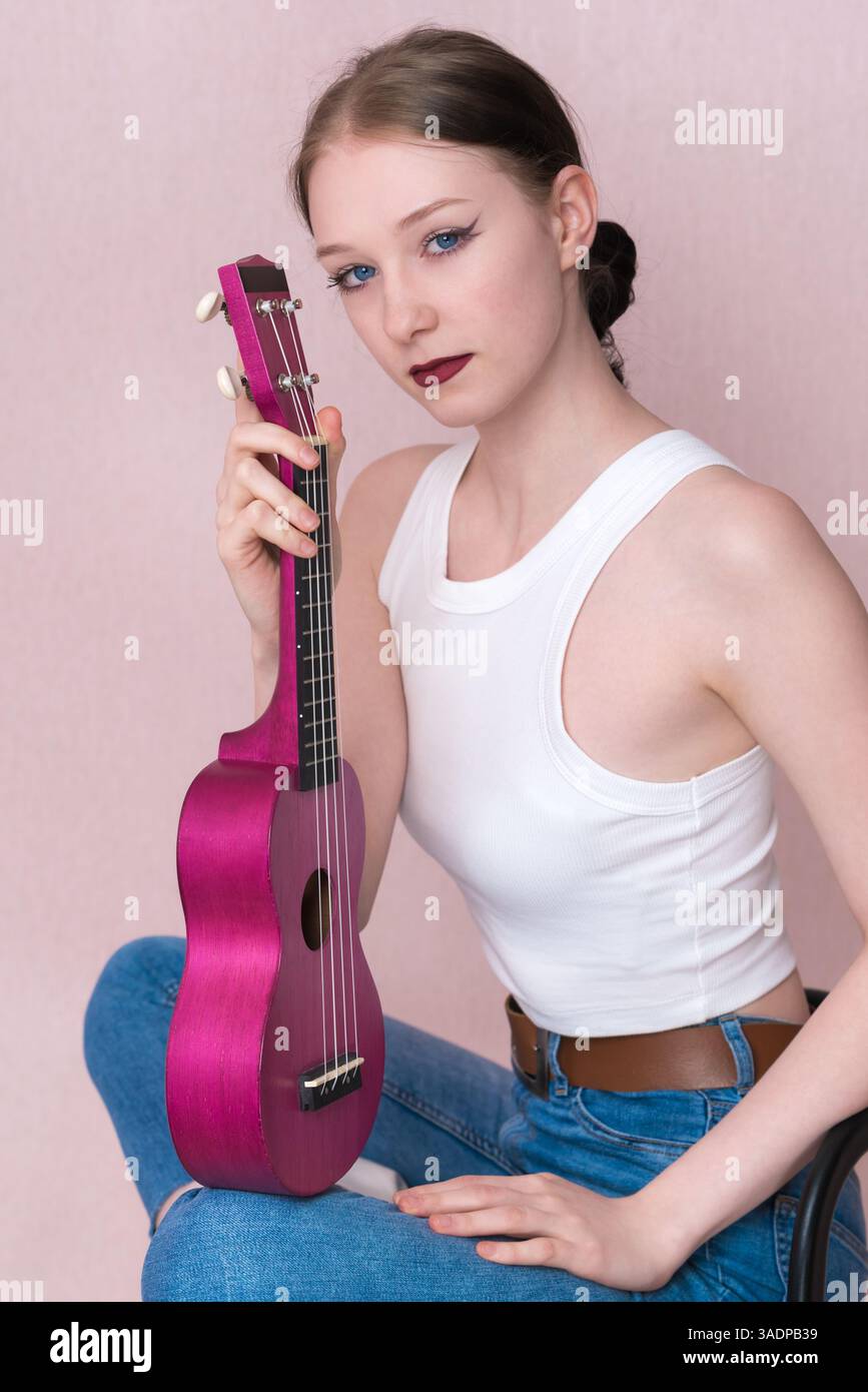Beautiful young female musician confidently holds ukulele vertically ...