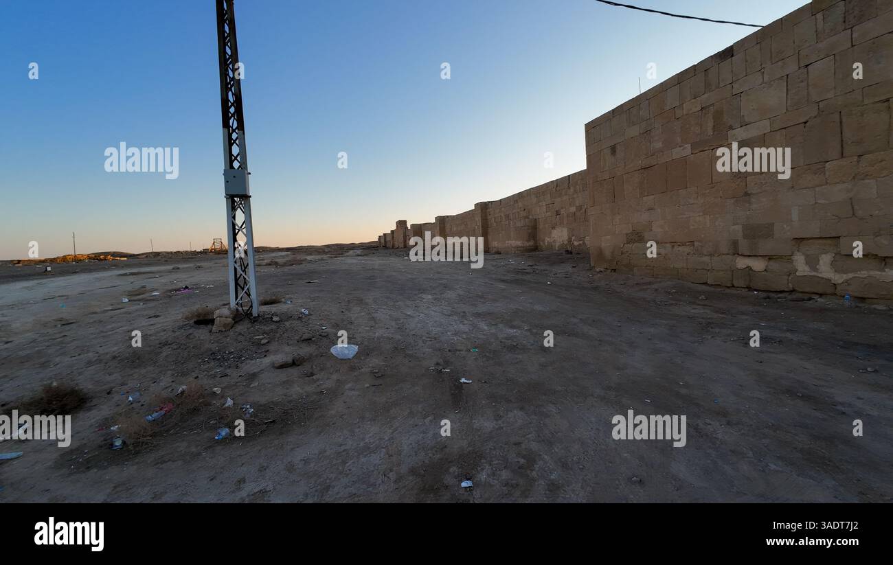 A deserted, barren landscape with a long stone wall and a metal utility ...