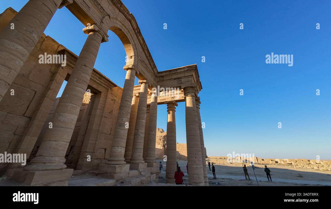 Ancient stone columns and arches under a clear blue sky, with people exploring the site Stock ...