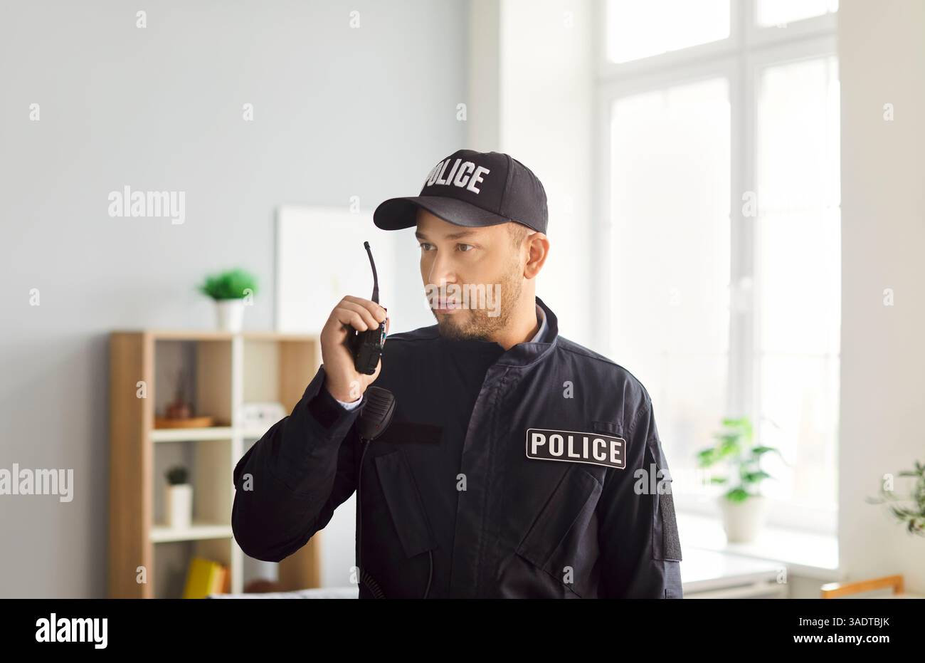Portrait of confident police officer standing indoors talking by walkie ...