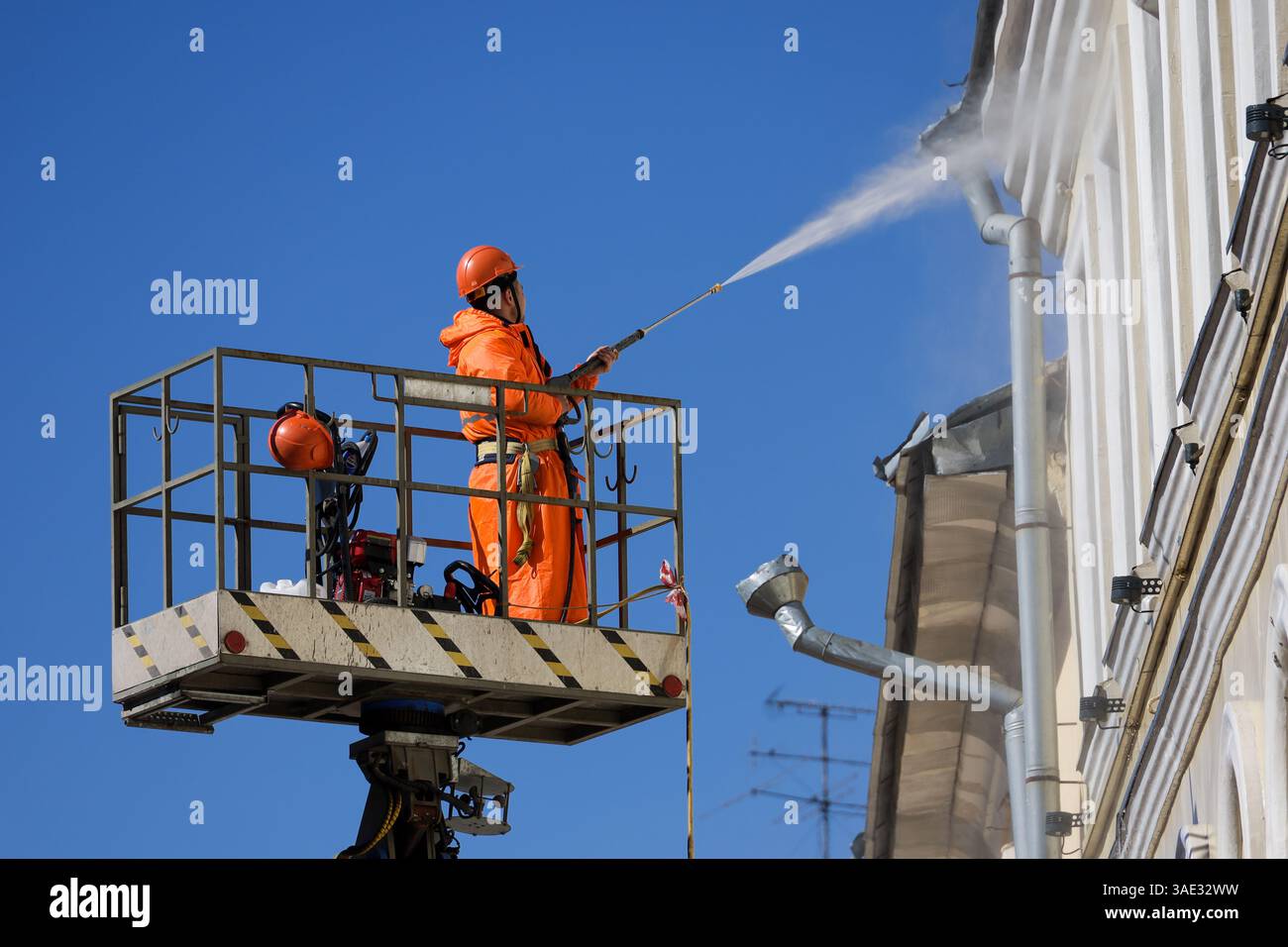 Worker in hydraulic lifting ramp washing the residential building wall ...