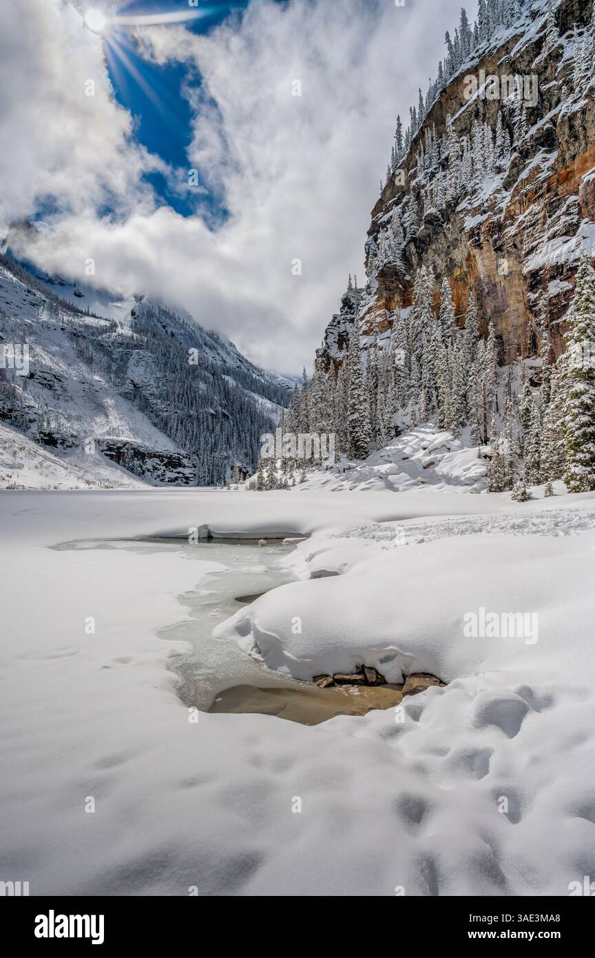 Winter view frozen Lake Louise and sun breaking through clouds in Banff ...