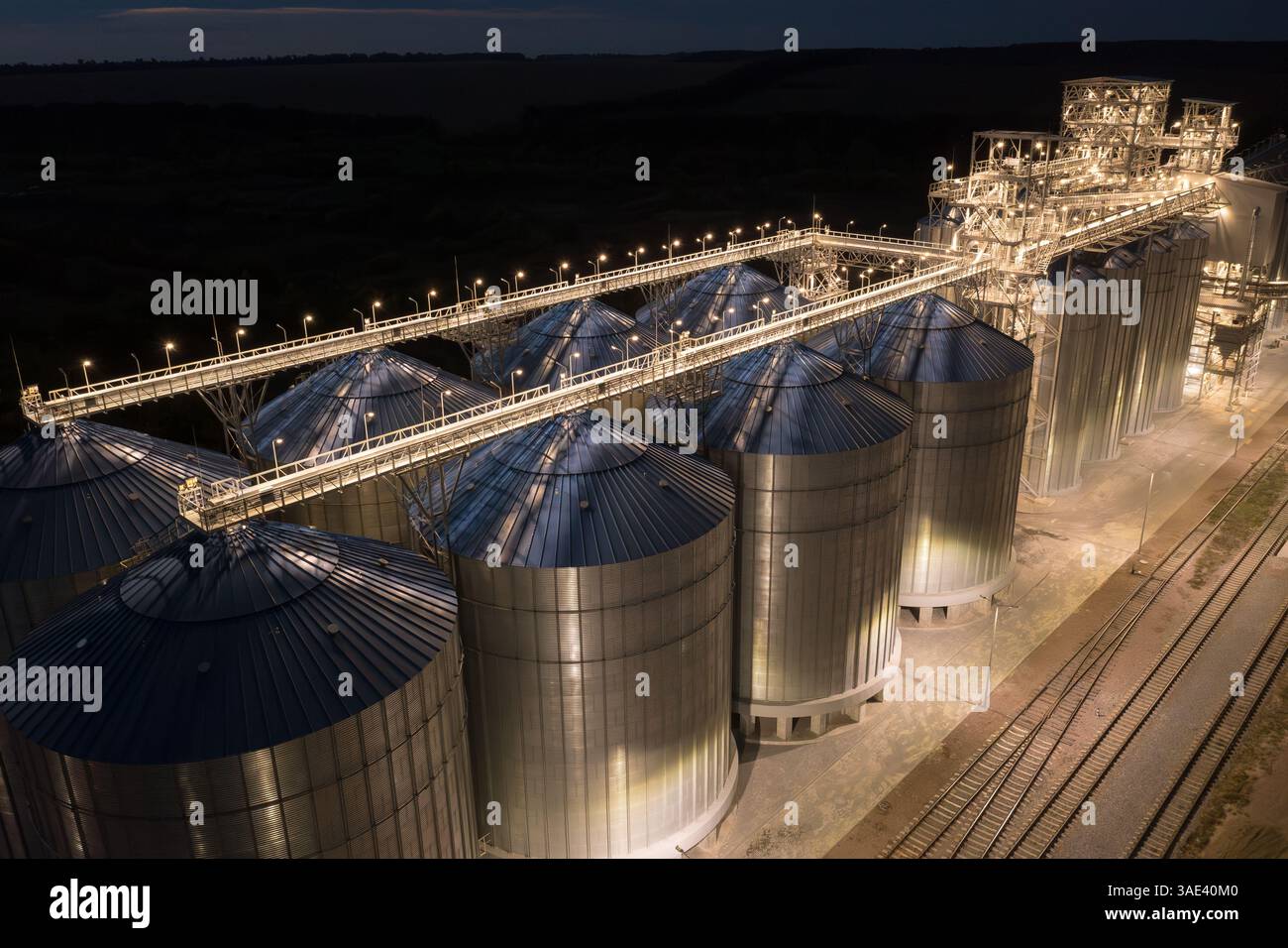 Aerial night view of illuminated grain silos and grain elevator facility in countryside, modern ...