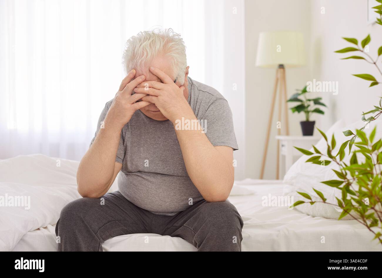 Senior elderly stressed man suffering from headache sitting on bed in ...
