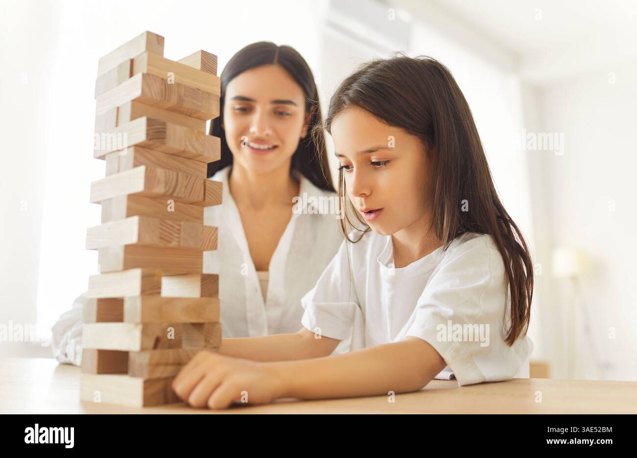 Girl and her mother are engaged in lively game of Jenga, showcasing their concentration and ...