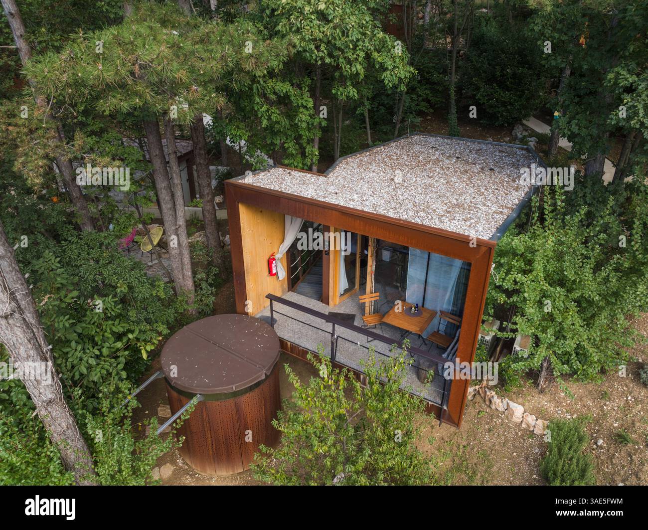 Aerial view of glamping hut with wooden deck and hot tub in forest ...