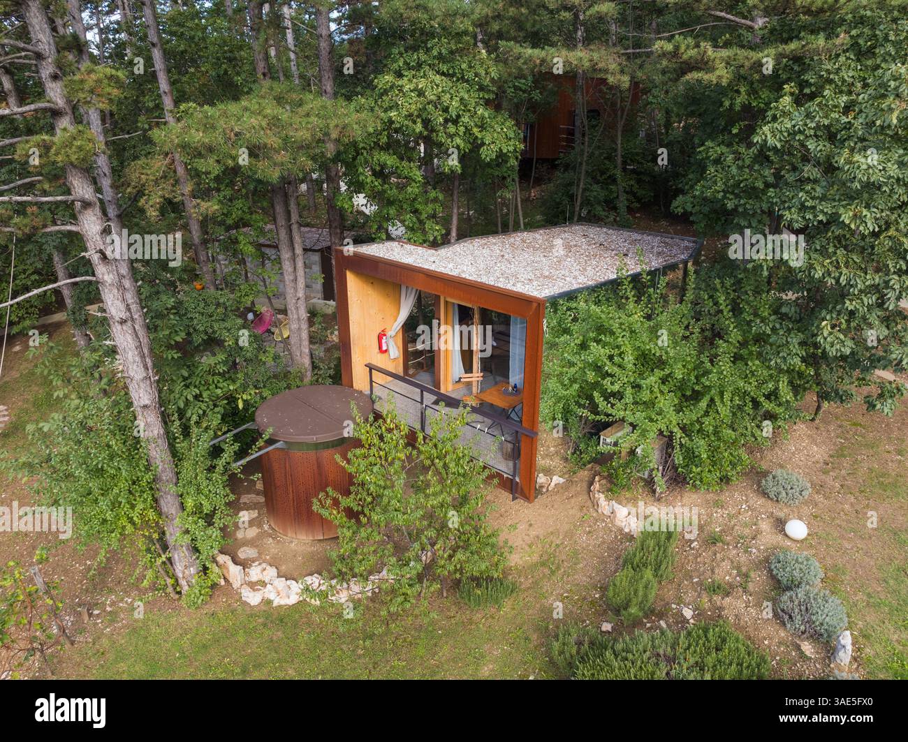 Aerial view of glamping hut with wooden deck and hot tub in forest ...