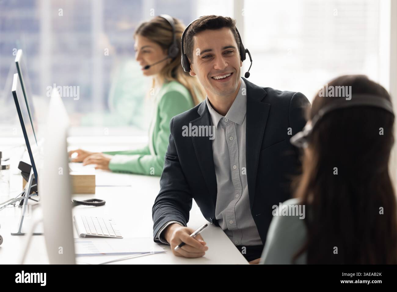 Happy contact center colleagues wearing headsets talking at workplace ...
