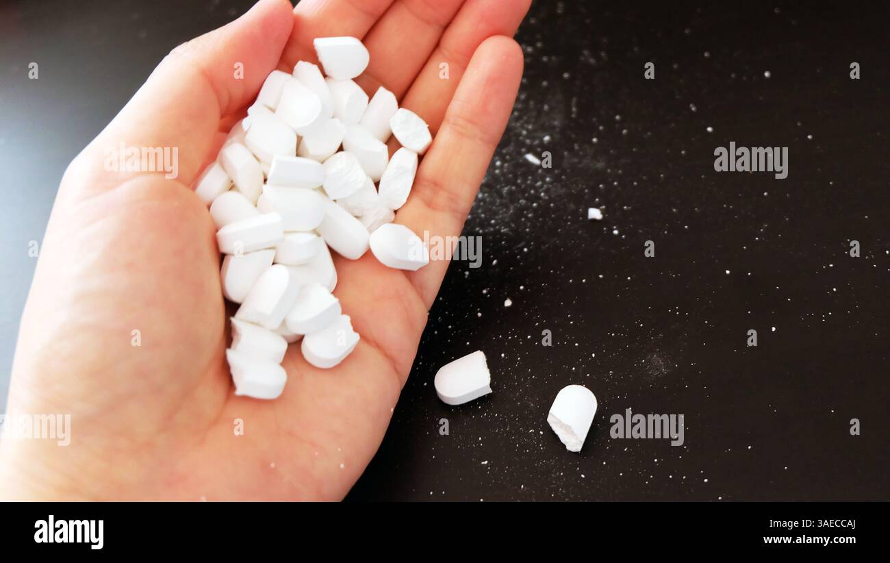 Hand with handful of white supplement tablets, crushed into half. With ...