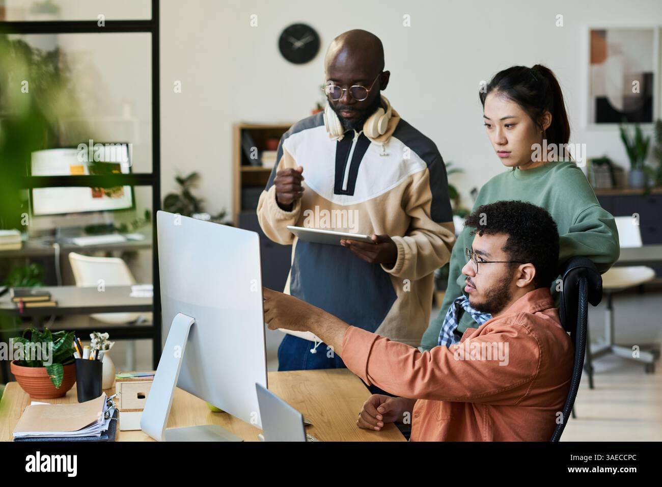 Group of young colleagues looking at screen of desktop computer while ...