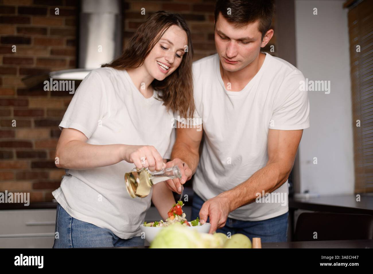 In cozy kitchen, man and woman prepare fresh and healthy vegetable salad together, enjoying ...