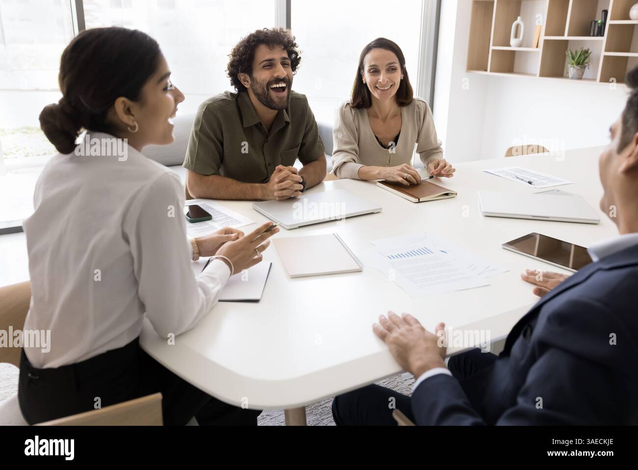 Four workmates attend group briefing laughing, joking gathered in ...
