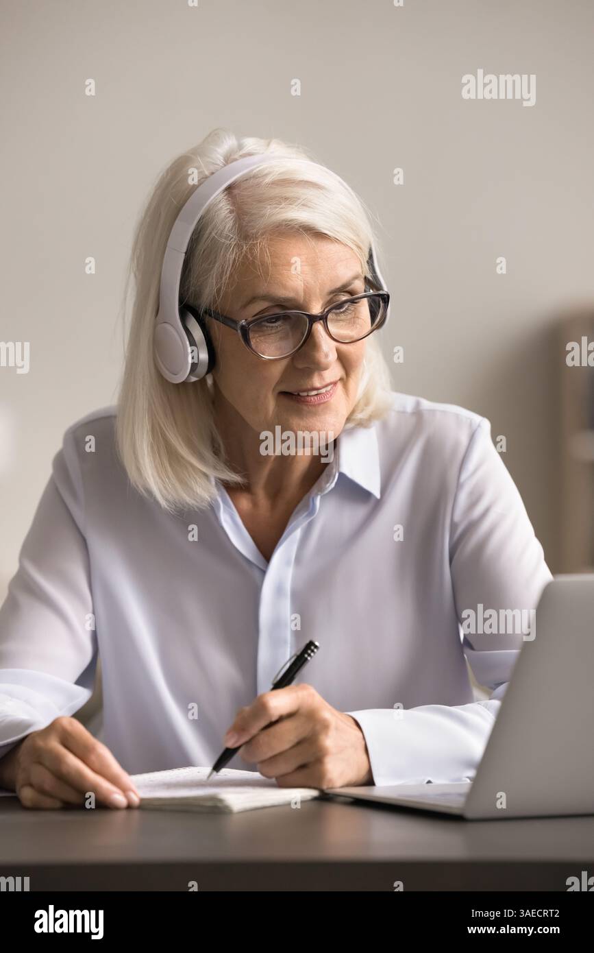 Interested older woman enjoy elearning with headphones on using ...