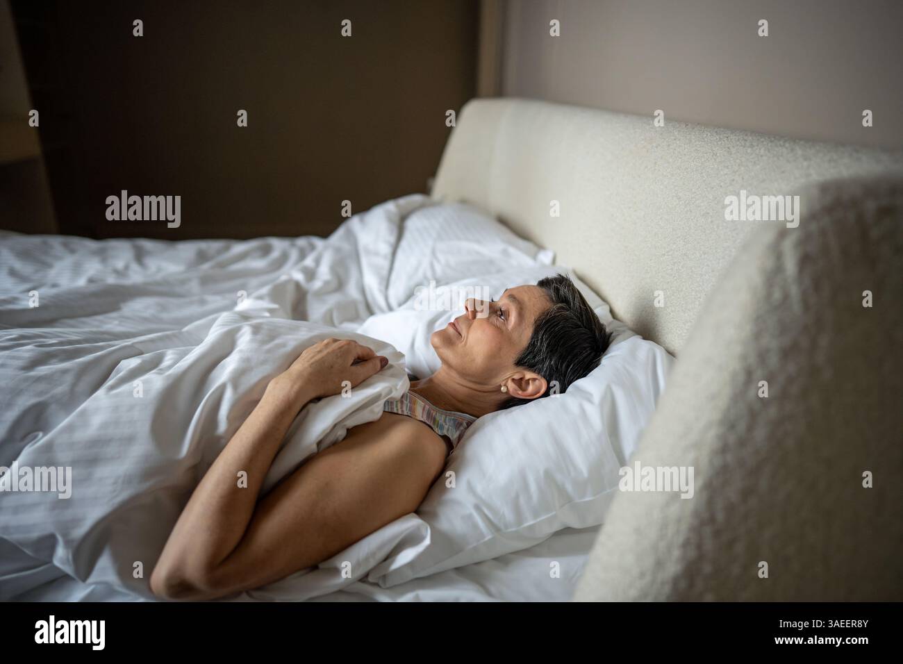 Tired mature woman lost in thoughts, staring at ceiling in bed, mental struggles with loneliness ...