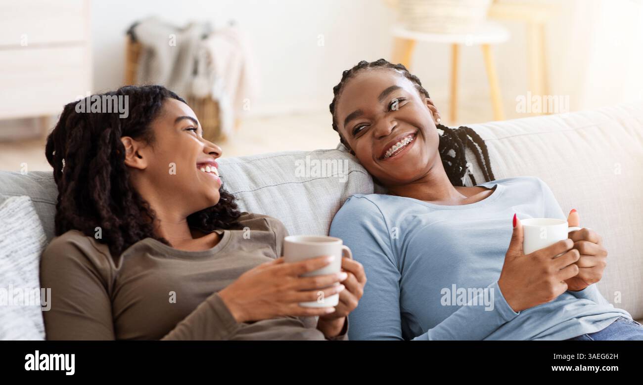Relaxed black ladies drinking tea, talking while resting on couch Stock ...