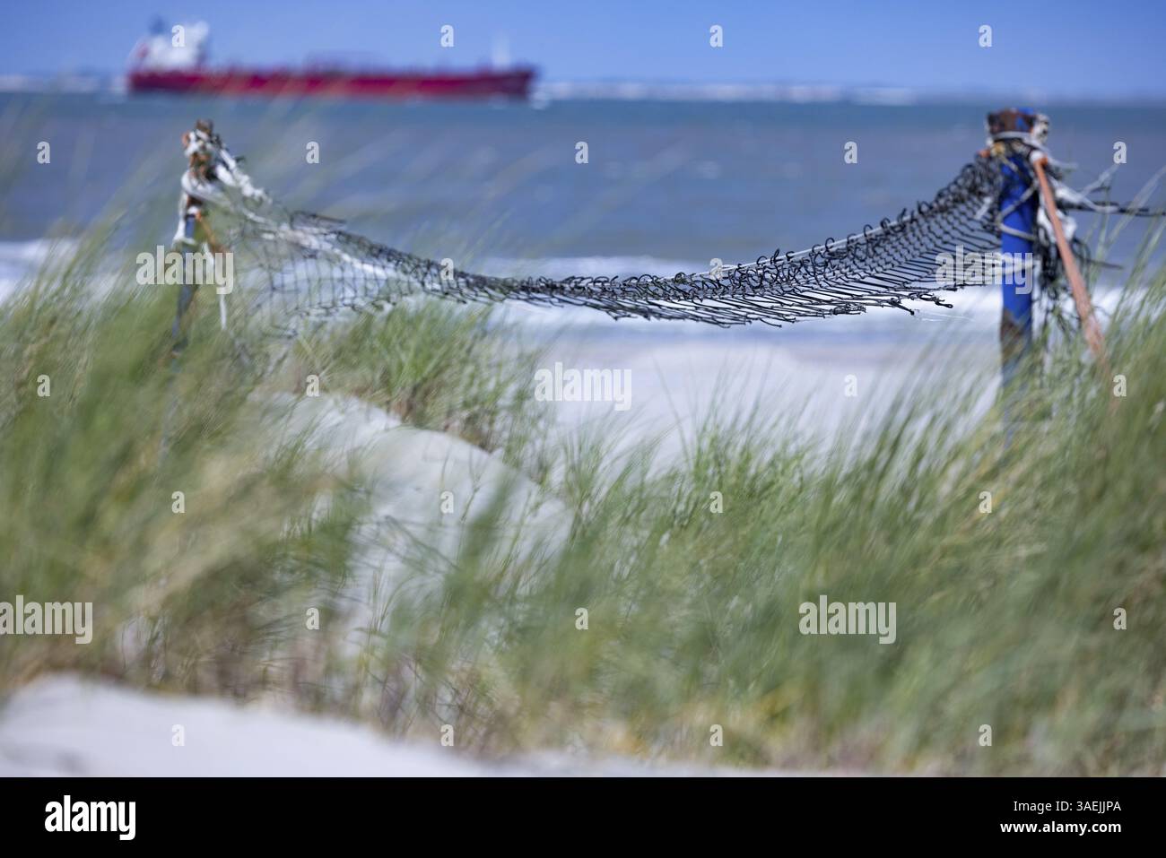 Old, weathered volleyball net in front of grasses on the beach, a ship ...
