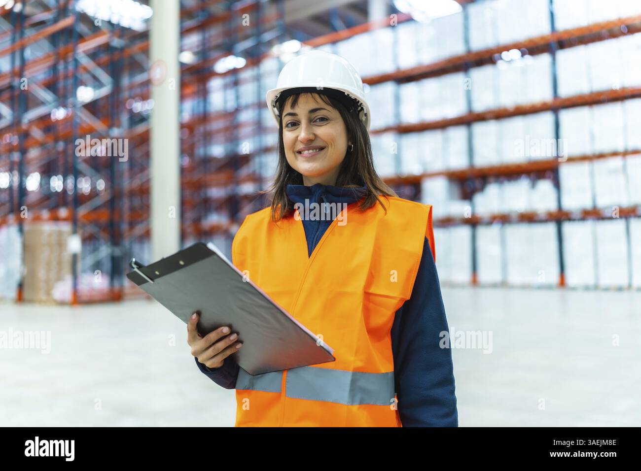 Warehouse worker wearing safety vest and helmet smiling and holding ...