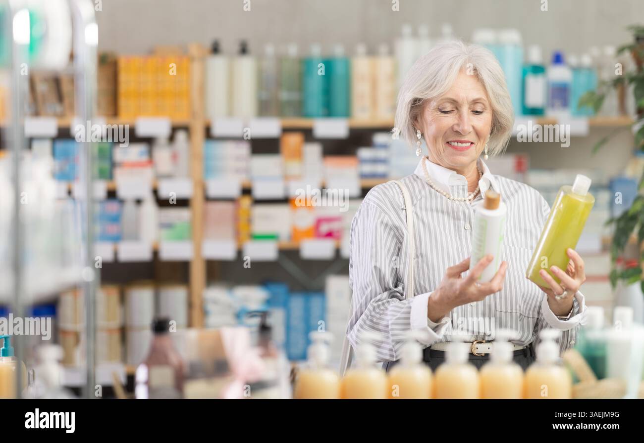 Elderly female shopper in summer clothes chooses medicated shampoo at ...