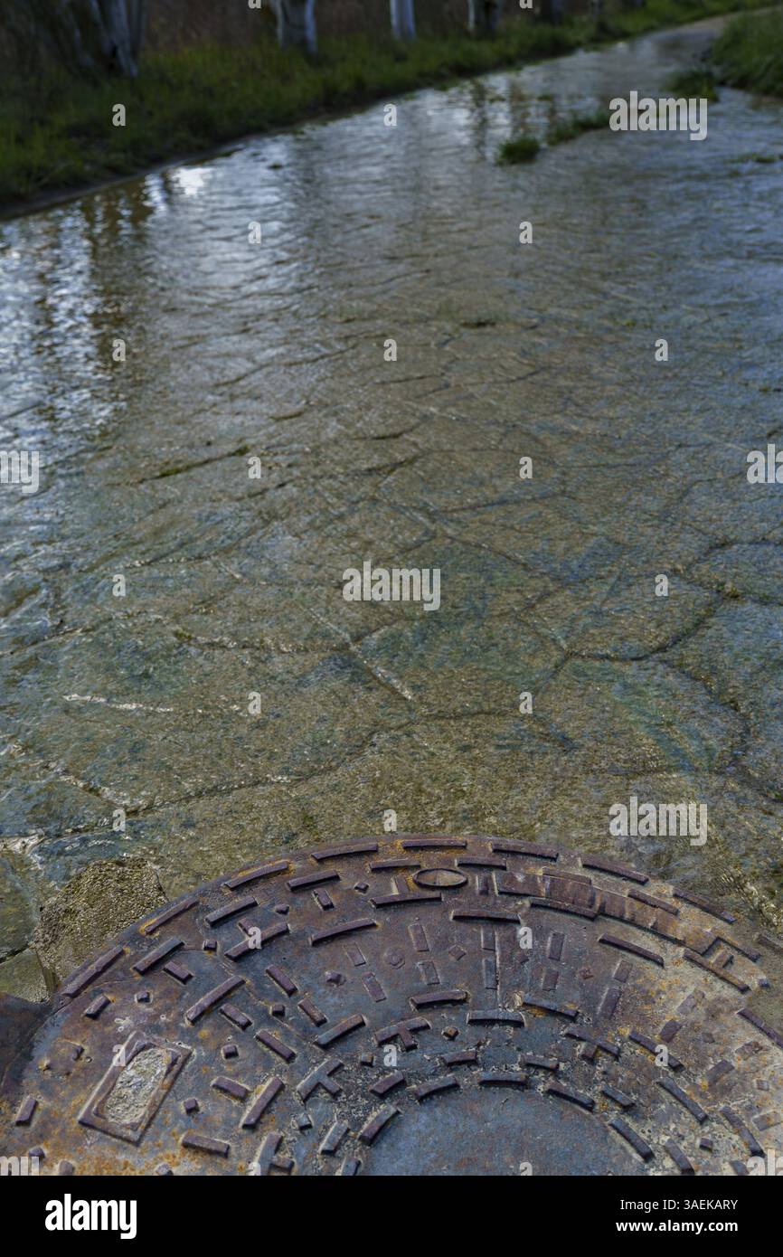Damaged manhole cover in a city street spilling water Stock Photo - Alamy