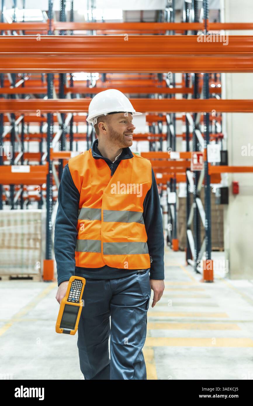 Warehouse worker wearing safety vest and helmet walking through ...