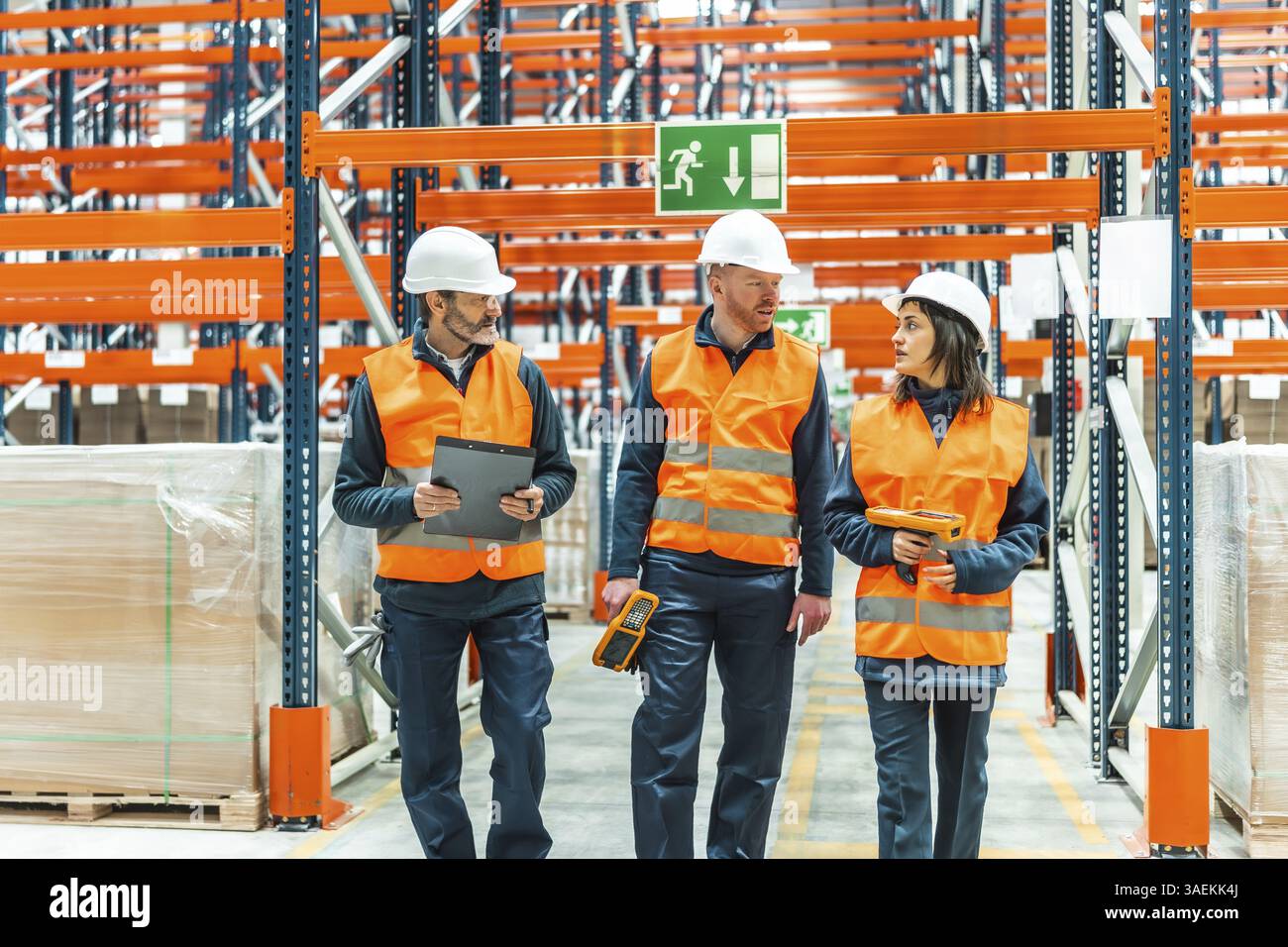 Warehouse workers walking through large distribution center, using ...