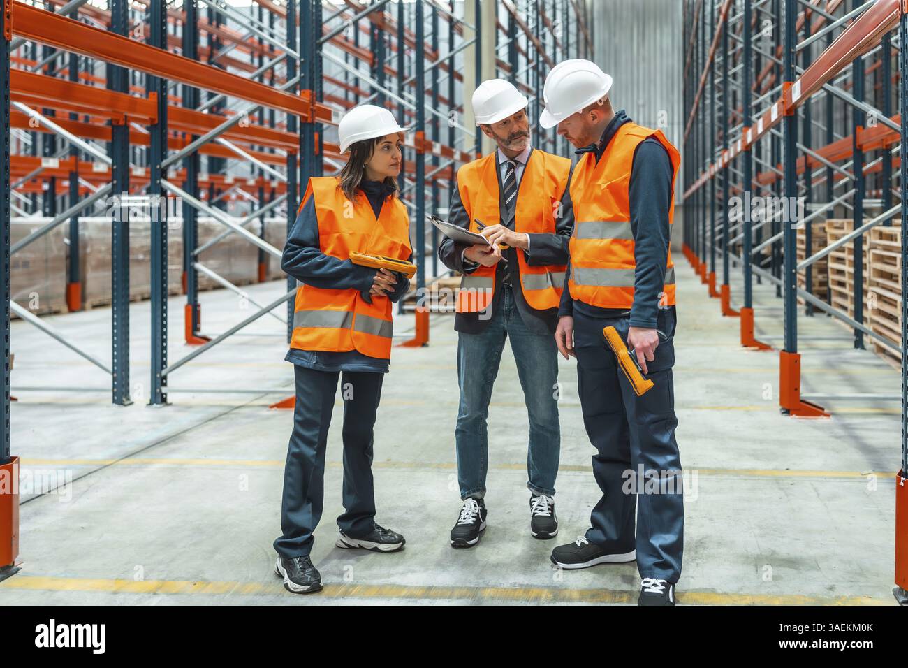 Warehouse workers and their manager are discussing logistics while holding barcode scanners in a ...