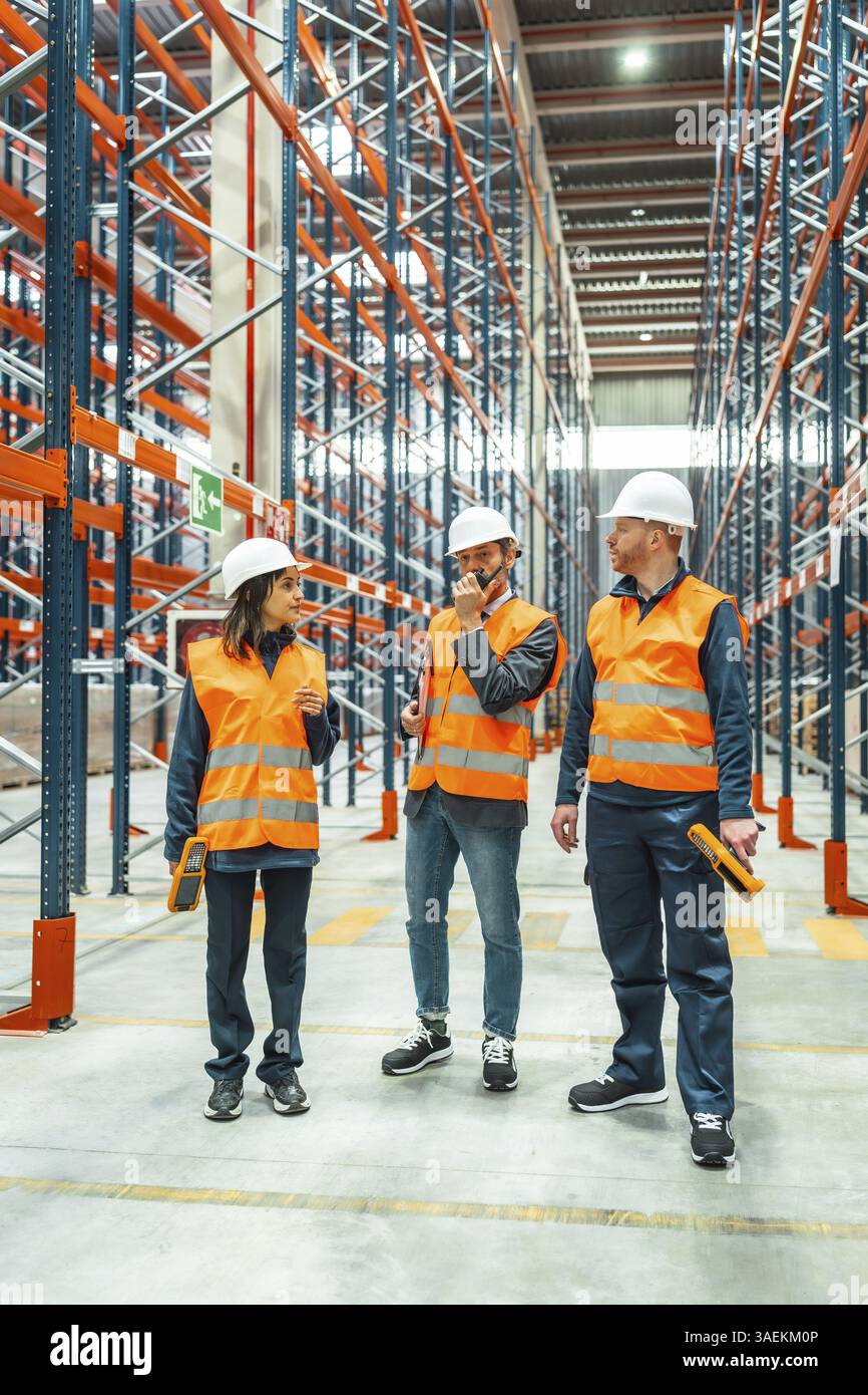 Warehouse workers wearing safety vests and helmets are discussing ...