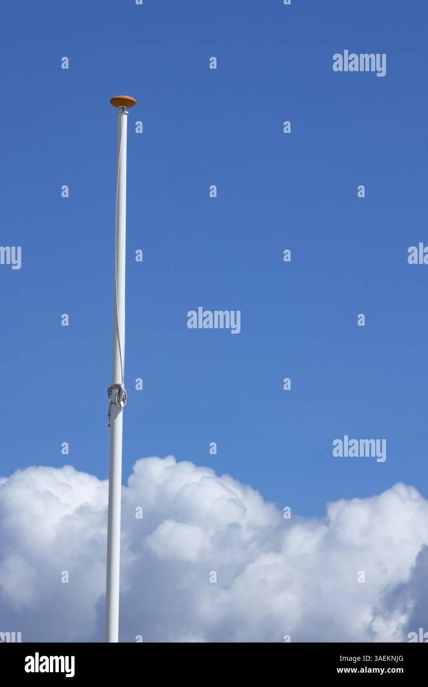 A white flagpole rises into a clear blue sky in front of a large ...