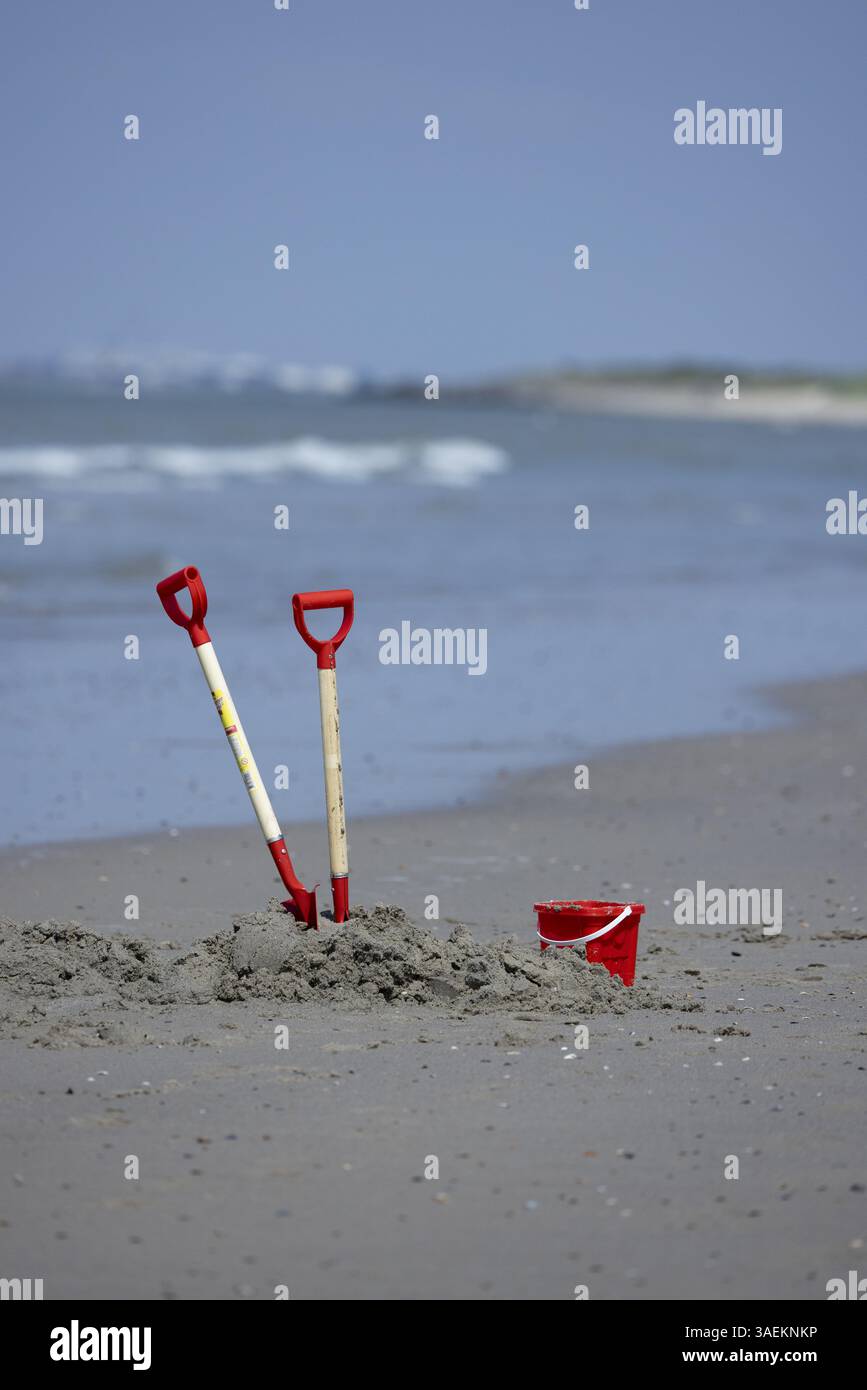 Two red shovels and a bucket in the sand on the beach in front of a ...