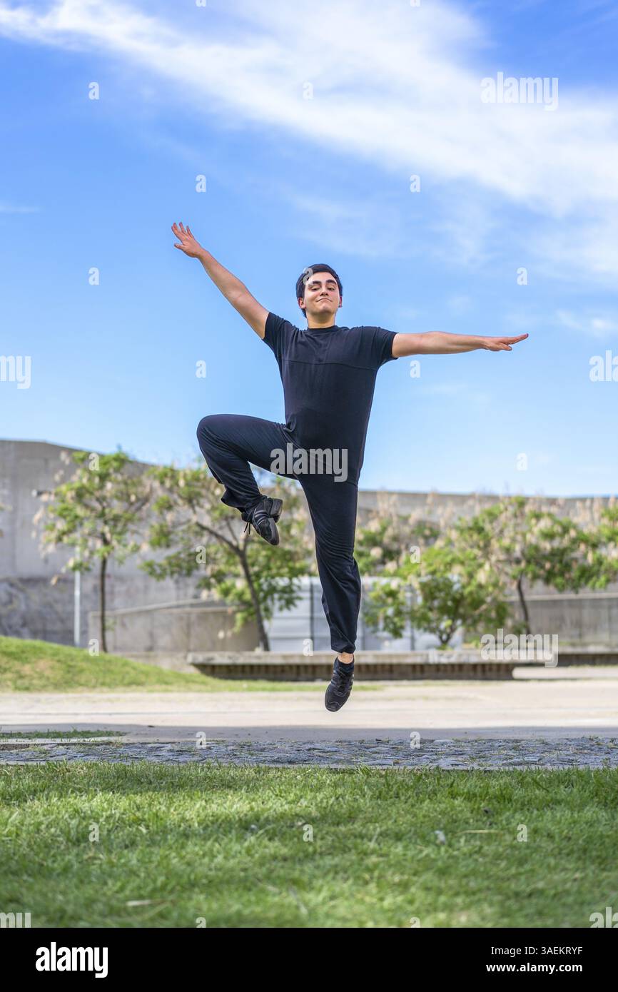 Dynamic young man leaping with joy in a green park under a blue sky ...