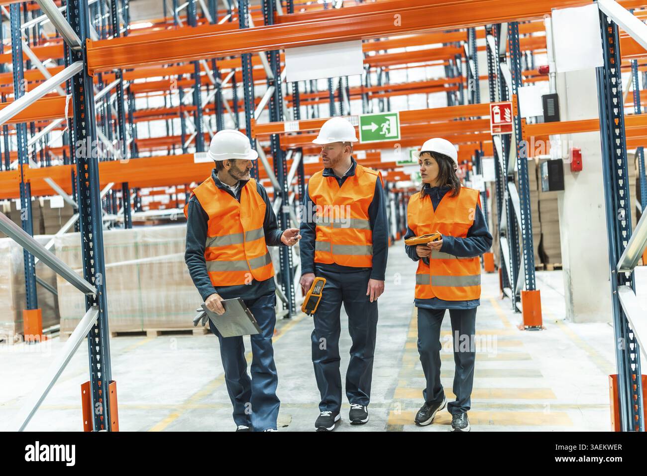 Warehouse workers wearing safety vests and helmets are walking through ...