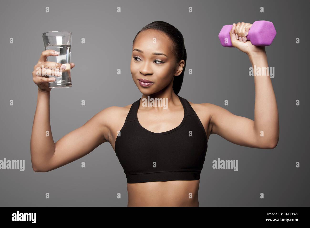 Beautiful healthy black asian woman with glass of water and dumbbell ...